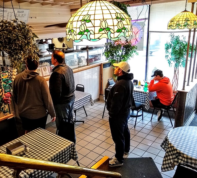 The line forms under vintage Tiffany-style lamps, where hungry patrons wait patiently for their turn at cheesesteak nirvana.