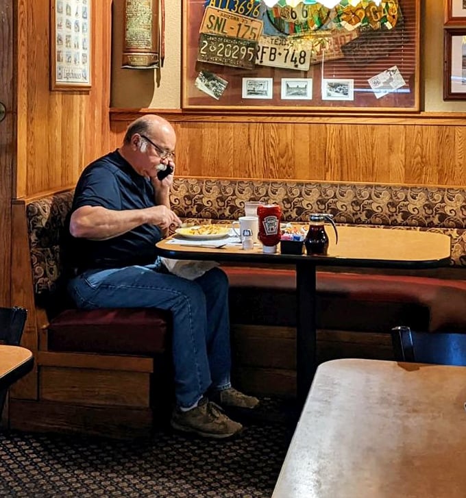 The quintessential diner experience: a regular enjoying his breakfast in a wood-paneled booth beneath vintage license plates – Norman Rockwell would approve.