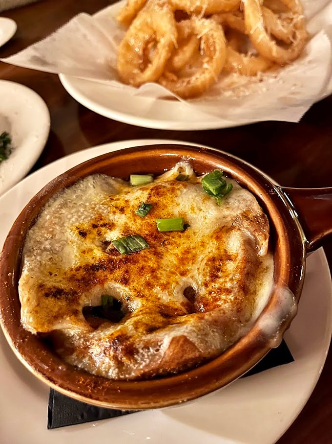 French onion soup that's achieved cult status – a bubbling cauldron of sweet onions and savory broth beneath a blanket of melted cheese that stretches with each spoonful.