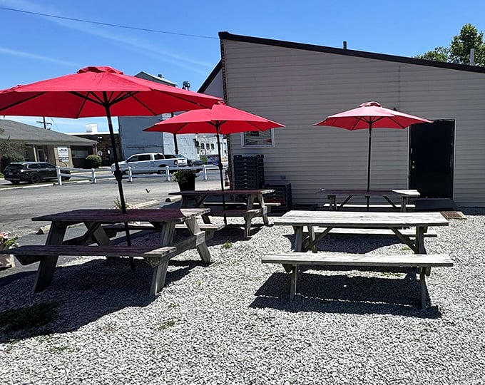 Red umbrellas dot the gravel patio like cherry tops on sundaes, offering shade for those who prefer their burgers with a side of sunshine.