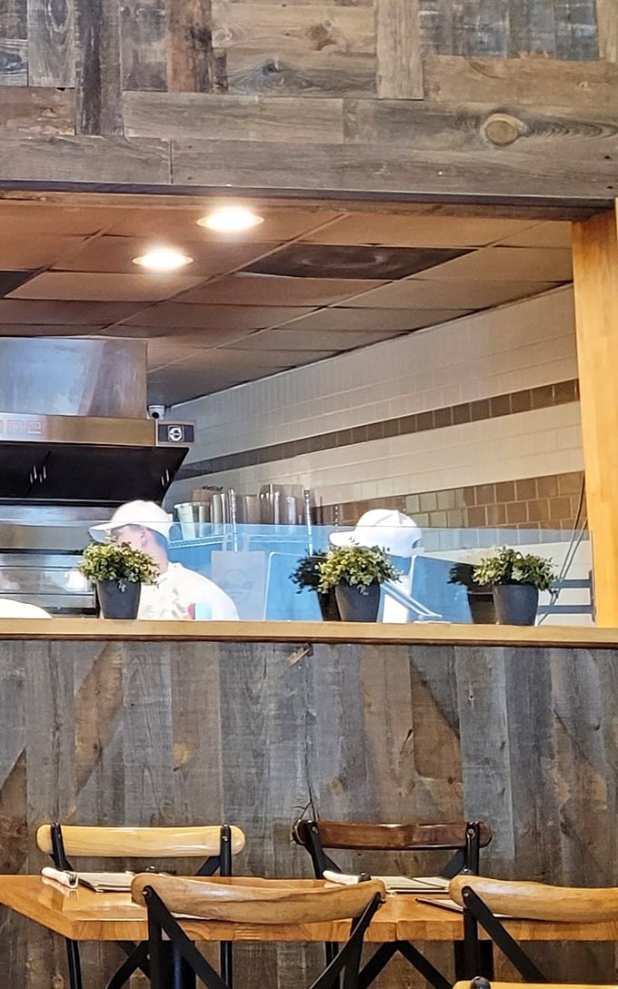 The open kitchen concept lets you witness pizza artistry in action. Those chefs aren't just cooking—they're performing delicious theater behind reclaimed wood.