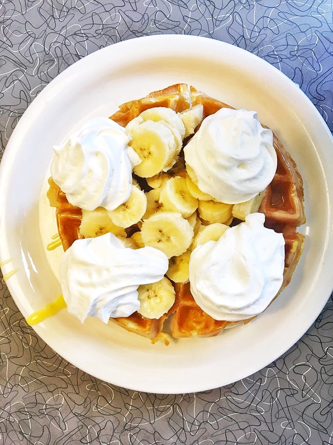 A Belgian waffle crowned with bananas and whipped cream—breakfast that boldly crosses the line into dessert territory without apology.