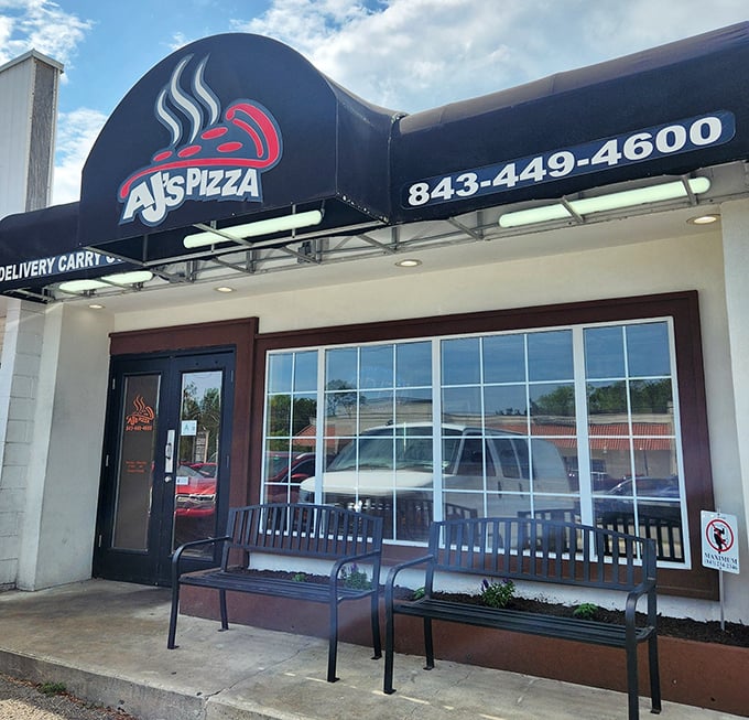 The unassuming storefront of AJ's Pizza beckons with its simple black awning and welcoming benches – proof that culinary treasures often hide in plain sight.