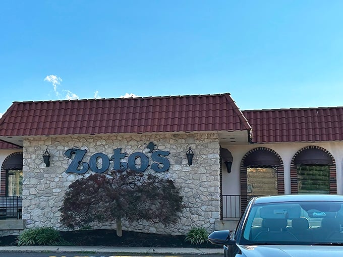 The stone facade and burgundy roof of Zoto's Diner stands like a culinary lighthouse, beckoning hungry travelers with promises of comfort food that transcends the ordinary.