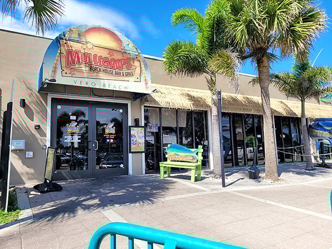 The cheerful facade of Mulligan's Beach House beckons like a tropical mirage, promising seafood treasures and ocean breezes just beyond those palm-flanked doors.