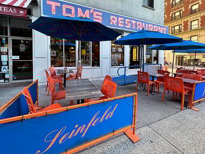 The iconic Tom's Restaurant sign glows like a beacon of comfort food hope, while the blue umbrellas create an inviting sidewalk oasis amid Manhattan's hustle.