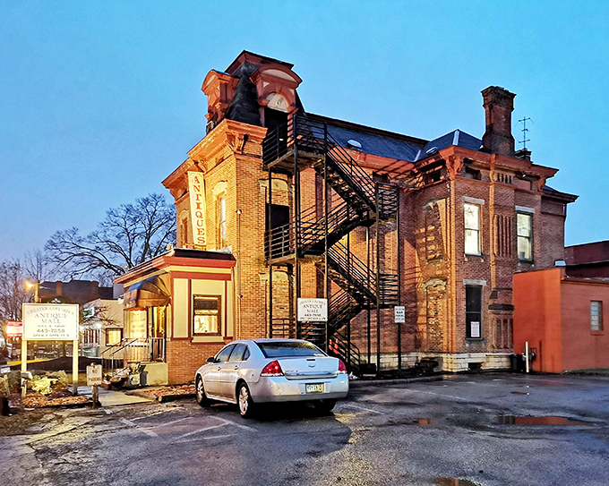 The historic brick building glows at twilight, its fire escape zigzagging dramatically against the façade like an architectural time machine waiting to transport visitors.