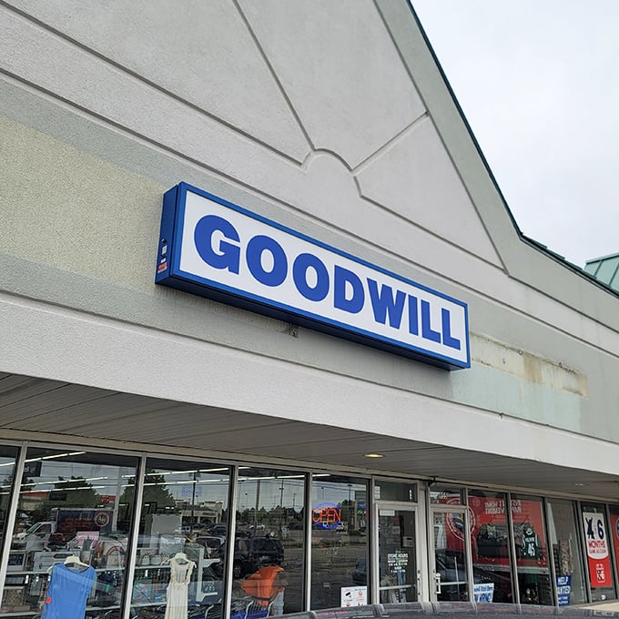 The iconic blue Goodwill sign beckons like a lighthouse for treasure hunters – promising adventures in secondhand splendor behind those unassuming walls.