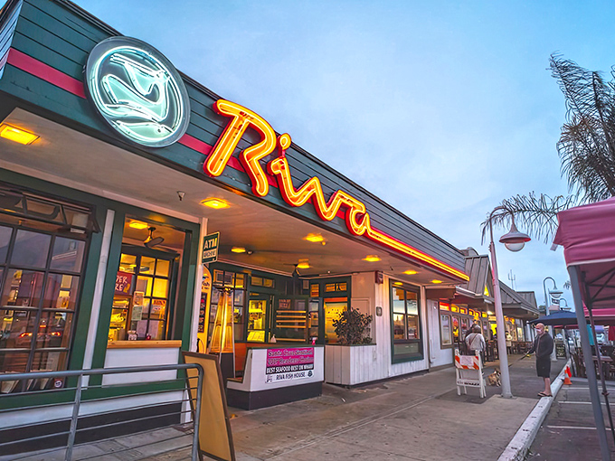 The neon glow of Riva's sign beckons seafood lovers like a lighthouse guiding hungry sailors home to port.