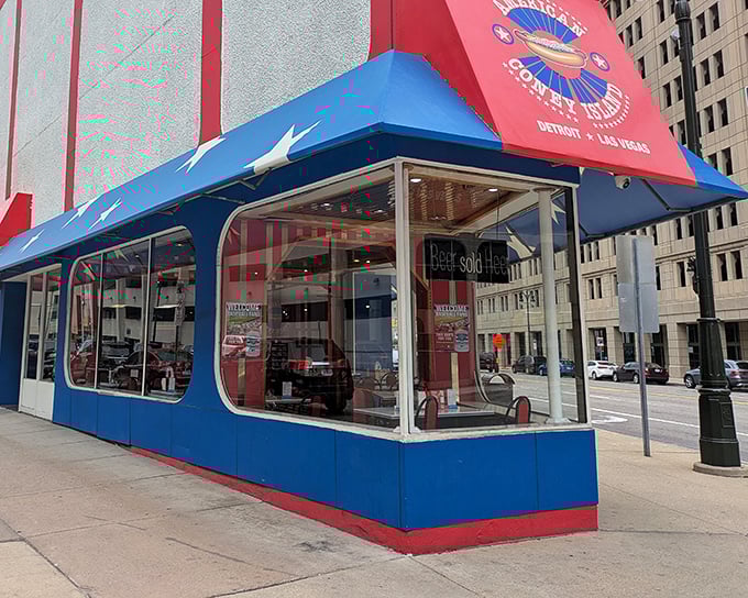 The patriotic awning of American Coney Island stands like a culinary lighthouse in downtown Detroit, beckoning hungry visitors with its red, white, and blue promise.