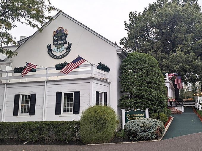 Colonial charm meets culinary excellence at the William Penn Inn's pristine white exterior, where American flags flutter like dinner invitations in the Pennsylvania breeze.