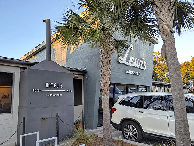 The sage-green exterior of Lewis Barbecue stands like a beacon of hope for hungry travelers, with its custom smoker proudly announcing "HOT GUTS" to passersby.