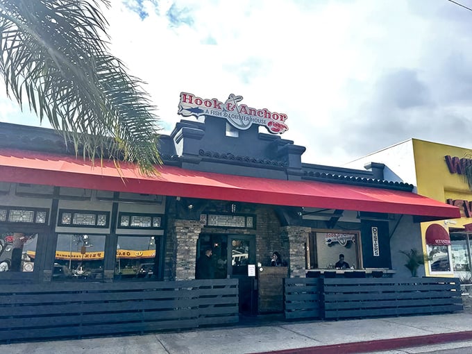 The bright red awning of Hook & Anchor beckons like a seafood siren against the California sky, promising maritime treasures within those unassuming walls.