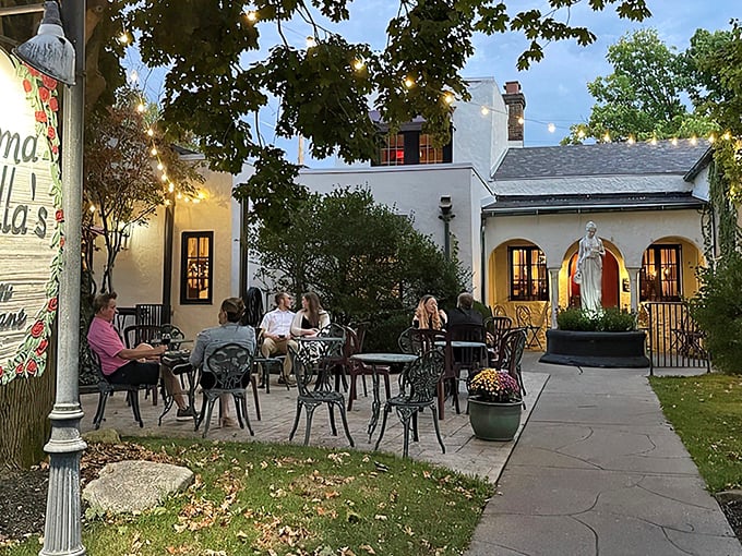 The enchanting patio at Mama Carolla's glows at twilight, where diners enjoy Italian cuisine under string lights and beside classical statuary.