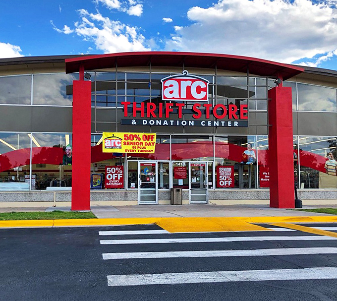 The red-trimmed facade of arc Thrift Store stands like a treasure chest waiting to be opened, promising adventures in secondhand splendor.