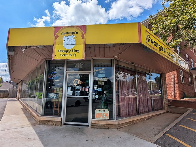 That bright yellow awning with the smiling cartoon pig is a beacon of barbecue hope—no frills, just the promise of smoky goodness waiting inside.