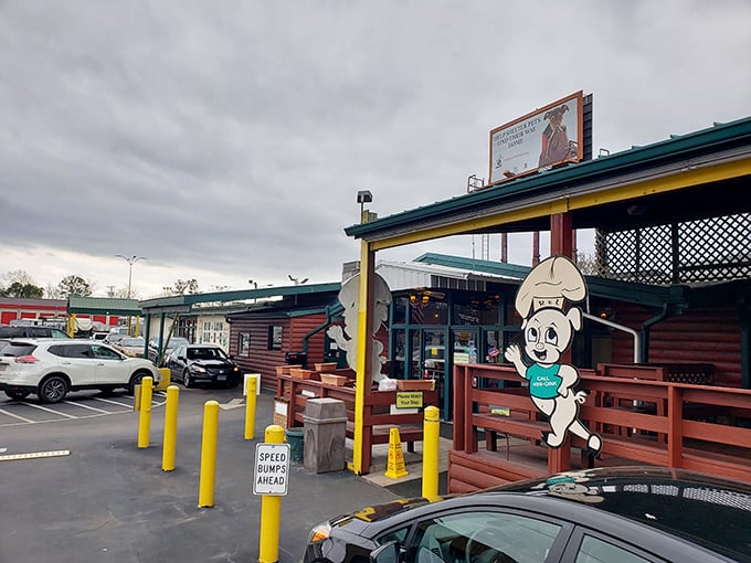The log cabin exterior of Rib & Loin welcomes hungry travelers with its cheerful chef mascot and yellow safety poles standing guard like sentinels protecting barbecue treasure.