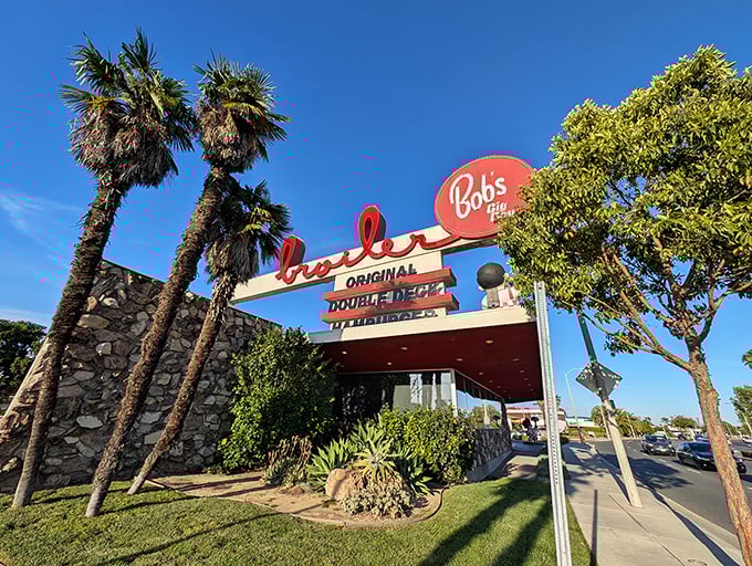 That iconic sign against the California blue sky isn't just advertising—it's a beacon of burger bliss promising nostalgic delights beneath those swaying palms.