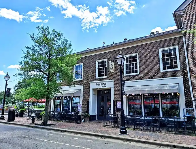 The charming brick façade of Mai Thai beckons from Old Town Alexandria's historic streets, promising culinary adventures behind those welcoming red awnings.