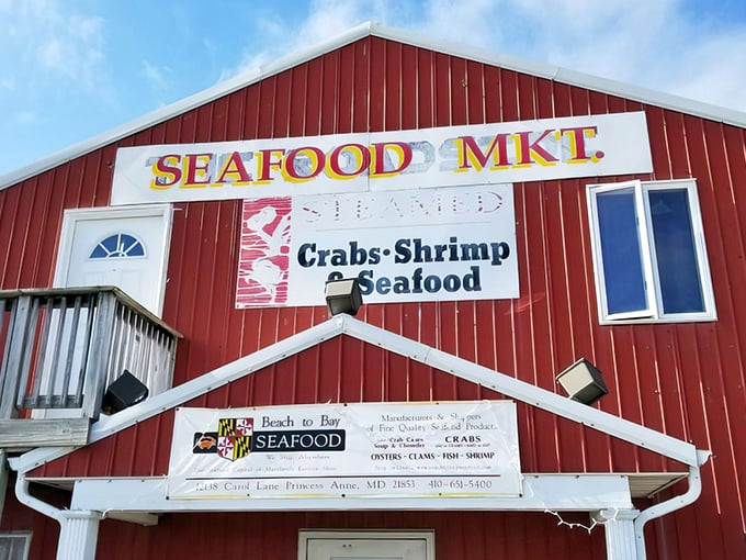 The iconic red barn exterior of Beach to Bay Seafood Company stands proudly against a Maryland sky, promising seafood treasures within its unassuming walls.