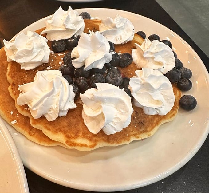 Blueberry pancakes topped with whipped cream clouds—proof that sometimes the simplest pleasures make the most profound breakfast statements.
