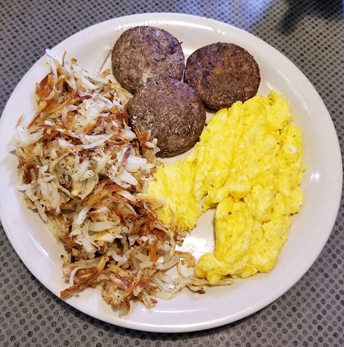The breakfast trinity—fluffy scrambled eggs, perfectly browned sausage patties, and hash browns that look like they've earned their crispy edges through years of dedication.