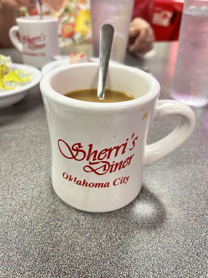 The simple white mug with "Sherri's Diner" in red script holds liquid motivation—no fancy latte art needed when the coffee's this good.