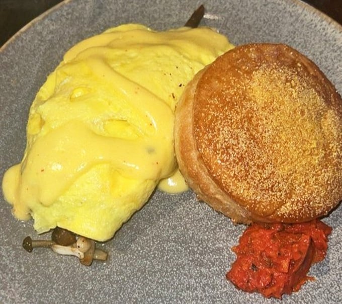 Sunshine-yellow eggs nestled against a golden English muffin with a splash of tomato jam – breakfast architecture at its finest.