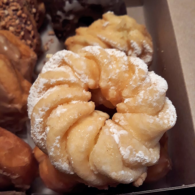 The flower-shaped cruller is architecture you can eat—delicate ridges dusted with powdered sugar, hiding a creamy custard center that's worth every calorie.