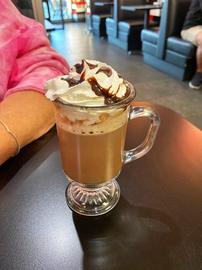 This hot chocolate isn't just a beverage, it's a dessert masquerading as a drink—topped with whipped cream and chocolate drizzle in a glass mug that means business.