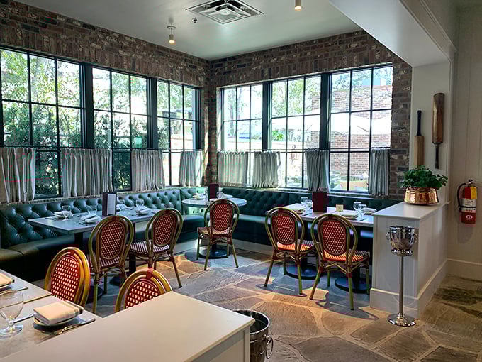 Sunlight streams through tall windows in this dining area where brick walls and tufted banquettes create the perfect backdrop for afternoon tea or evening cocktails.