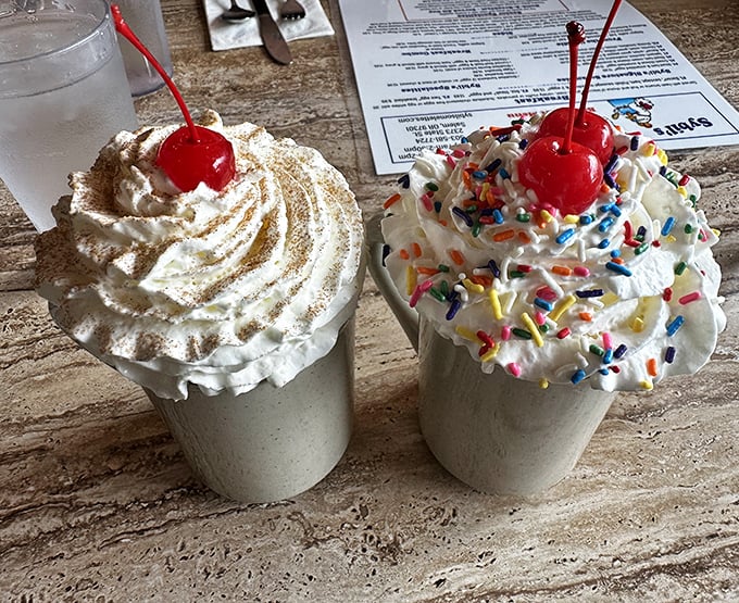 Milkshakes topped with whipped cream mountains and cherries—one classic, one festive with sprinkles—both guaranteed to bring smiles.