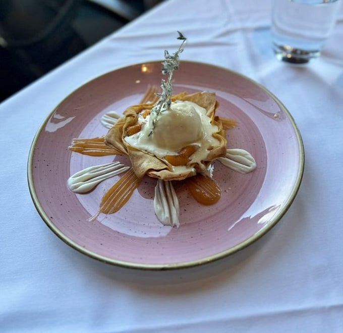 Dessert architecture that belongs in a museum – crispy phyllo cradling what appears to be ice cream, surrounded by artistic sauce flourishes.