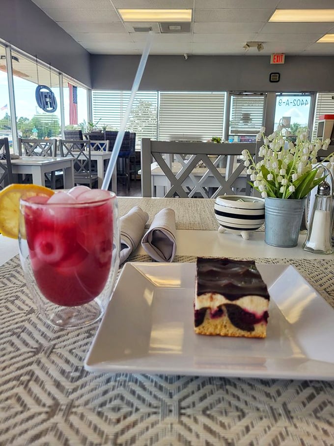 A slice of berry-studded cake alongside ruby-red lemonade—proof that sometimes the best vacation moments happen at a bakery table, not a beach.
