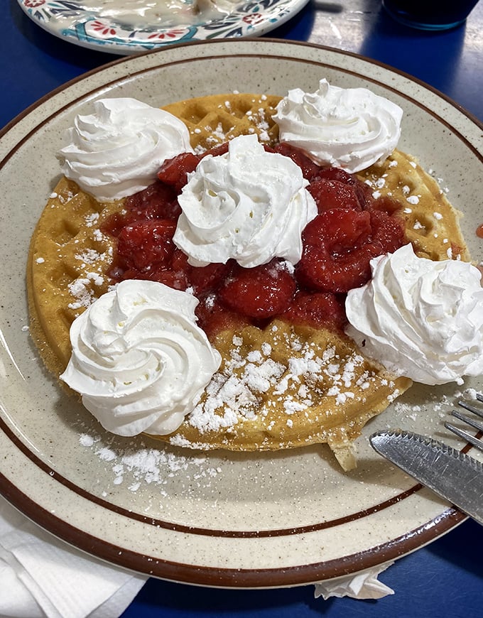 A waffle topped with strawberries and whipped cream rosettes that look almost too pretty to destroy with your fork.