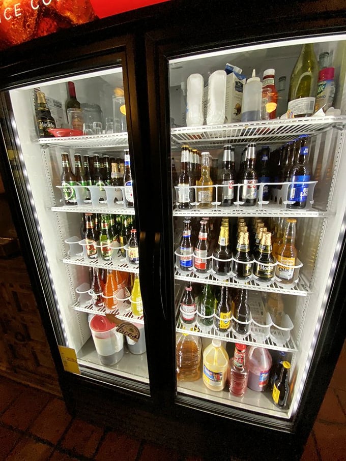 The beverage cooler stands ready like a United Nations of refreshment – Mexican sodas diplomatically sharing space with American favorites.