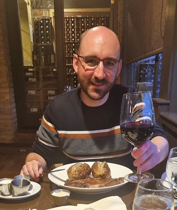 A dining companion enjoys the perfect pairing – a robust red wine alongside a steak that's clearly worth savoring slowly.