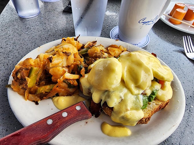 Eggs Benedict done right—hollandaise cascading down like a yellow waterfall of buttery goodness, with crispy potatoes standing by for the assist.