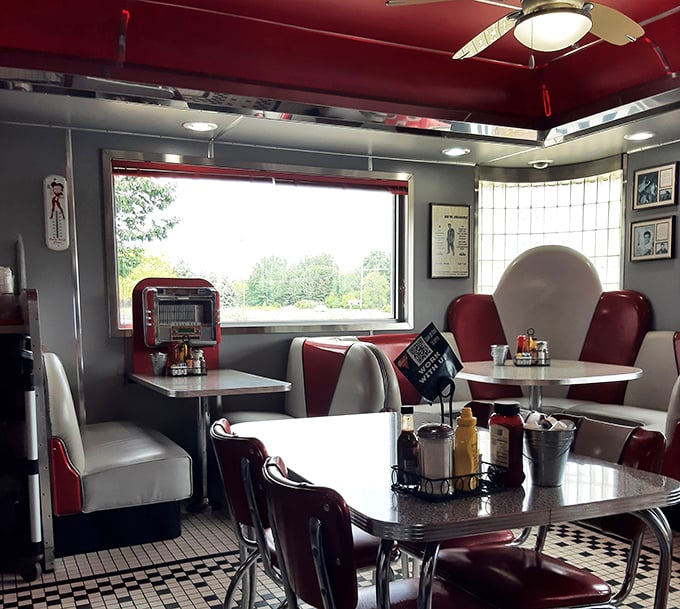 Sunlight streams through windows framing red and white booths, while vintage jukeboxes stand ready. Not just a meal, but a complete sensory experience.