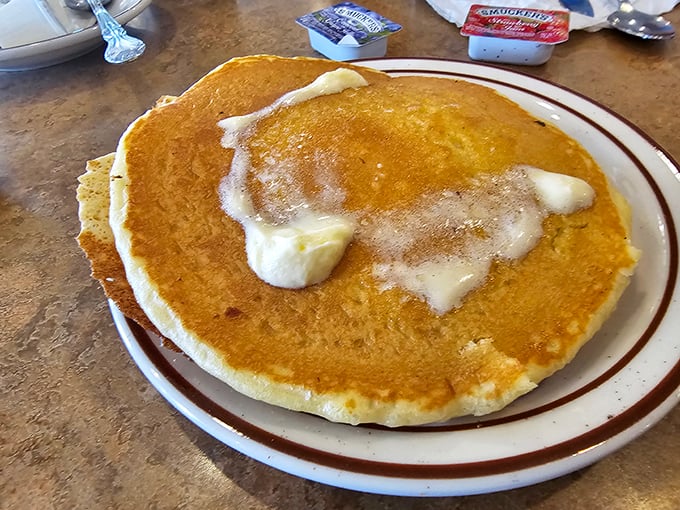 This pancake isn't just large—it's practically a circular mattress of fluffy goodness, melting butter creating little pools of heaven that no maple syrup could resist.