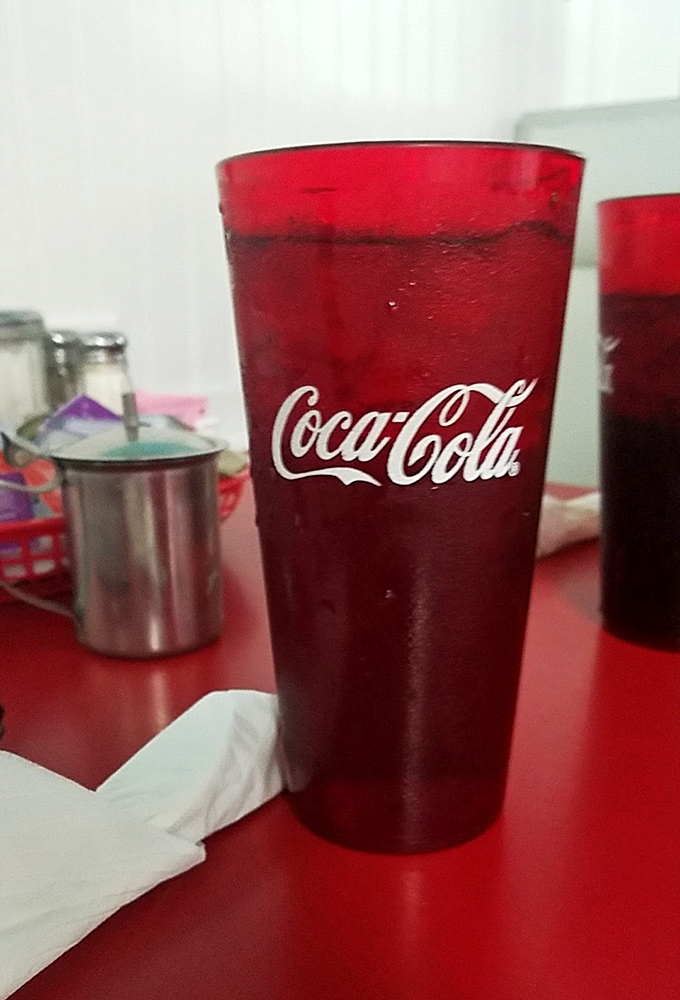 That classic red Coca-Cola glass—somehow making your soda taste better through the power of nostalgia and proper serving temperature.