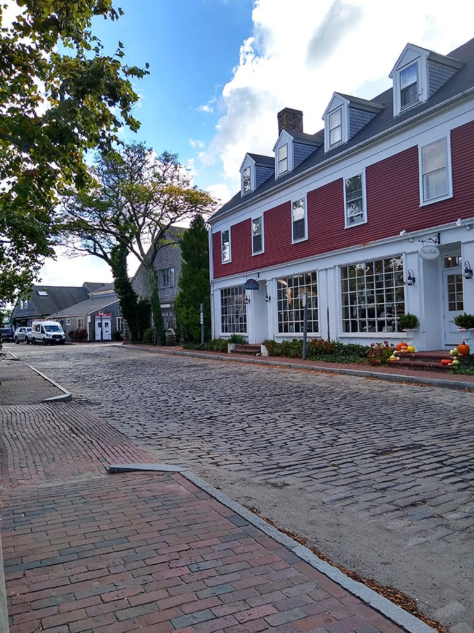 Cobblestone streets and brick sidewalks lead past classic Nantucket buildings where roses climb gray-shingled walls in perfect coastal New England style.