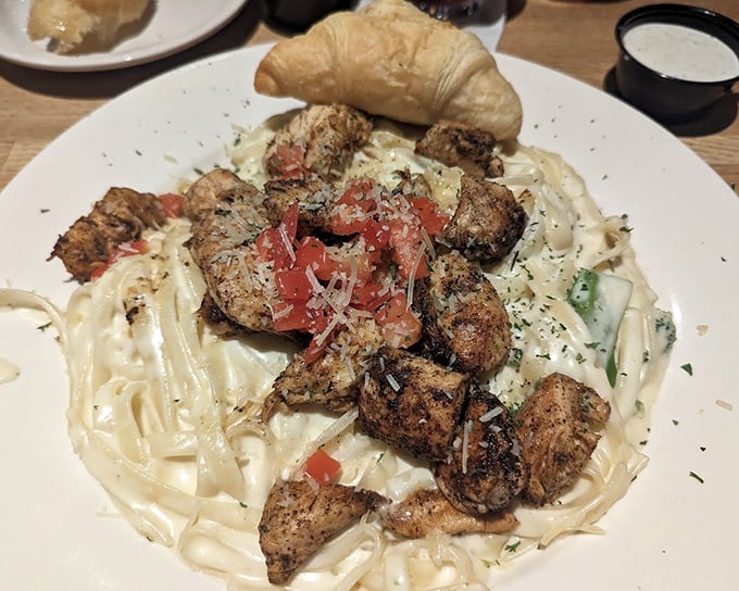 Fettuccine Alfredo crowned with grilled chicken and a buttery croissant—because sometimes you need carbs supporting your carbs supporting your protein.