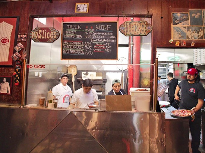 Behind the counter, the pizza ballet unfolds – practiced hands moving with the confidence that comes only from thousands of pies.