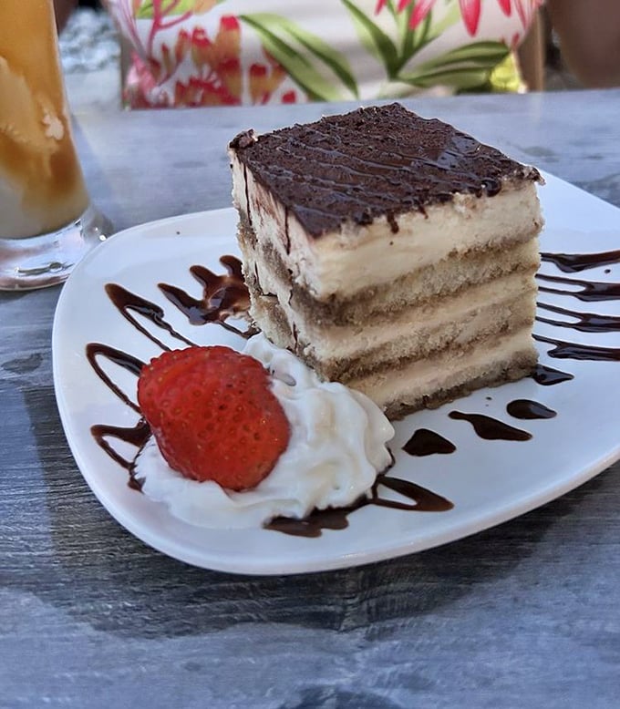 Tiramisu that's dressed better than most wedding guests—layers of coffee-soaked elegance topped with chocolate and a strawberry beret.