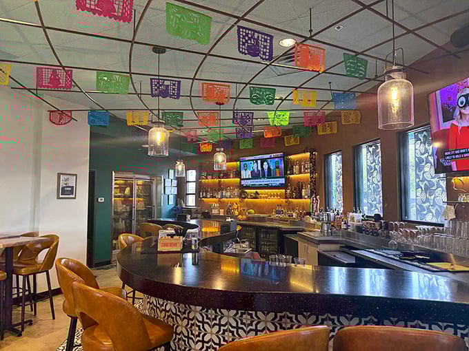 The bar doesn't just serve drinks – it showcases them, with bottles glowing like amber treasures and papel picado creating a ceiling of perpetual celebration.