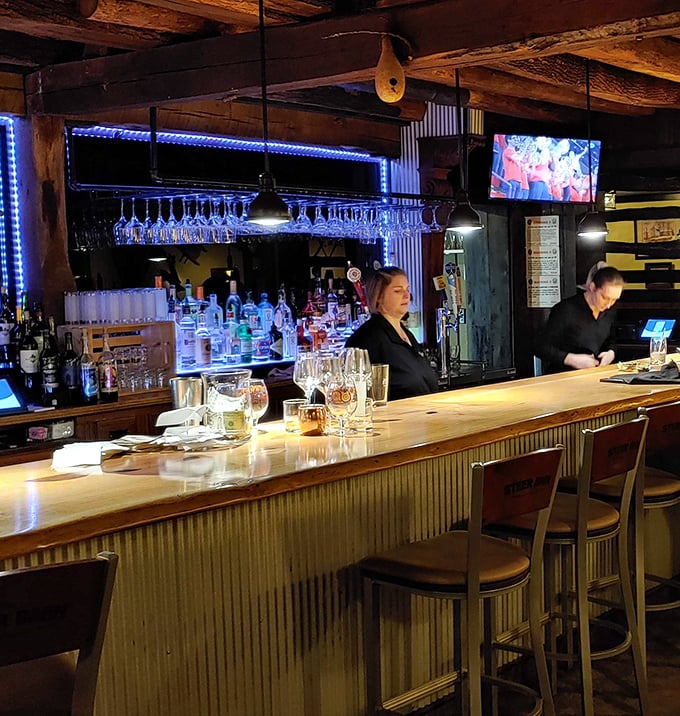 Behind the bar, where magic happens—skilled hands transform simple ingredients into complex cocktails under the warm glow of pendant lights and blue accents.