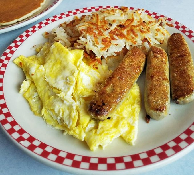 Breakfast trinity: eggs, sausage, and hash browns—the holy alliance that makes mornings bearable. Simple perfection on a red-rimmed plate.