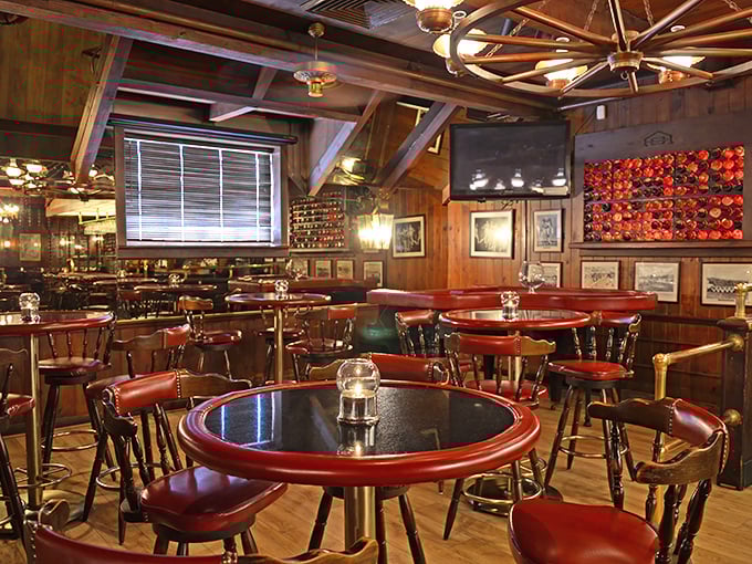 Round tables with burgundy trim create intimate dining islands in a sea of wood paneling—classic steakhouse design that never goes out of style.