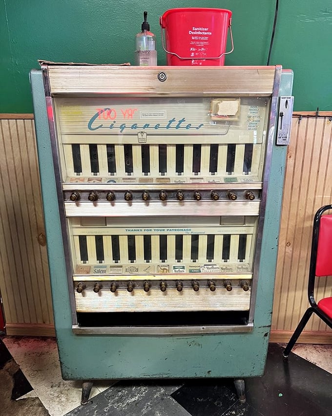 This vintage cigarette machine stands as a museum piece from another era, now repurposed beside modern hand sanitizer—old meets new.